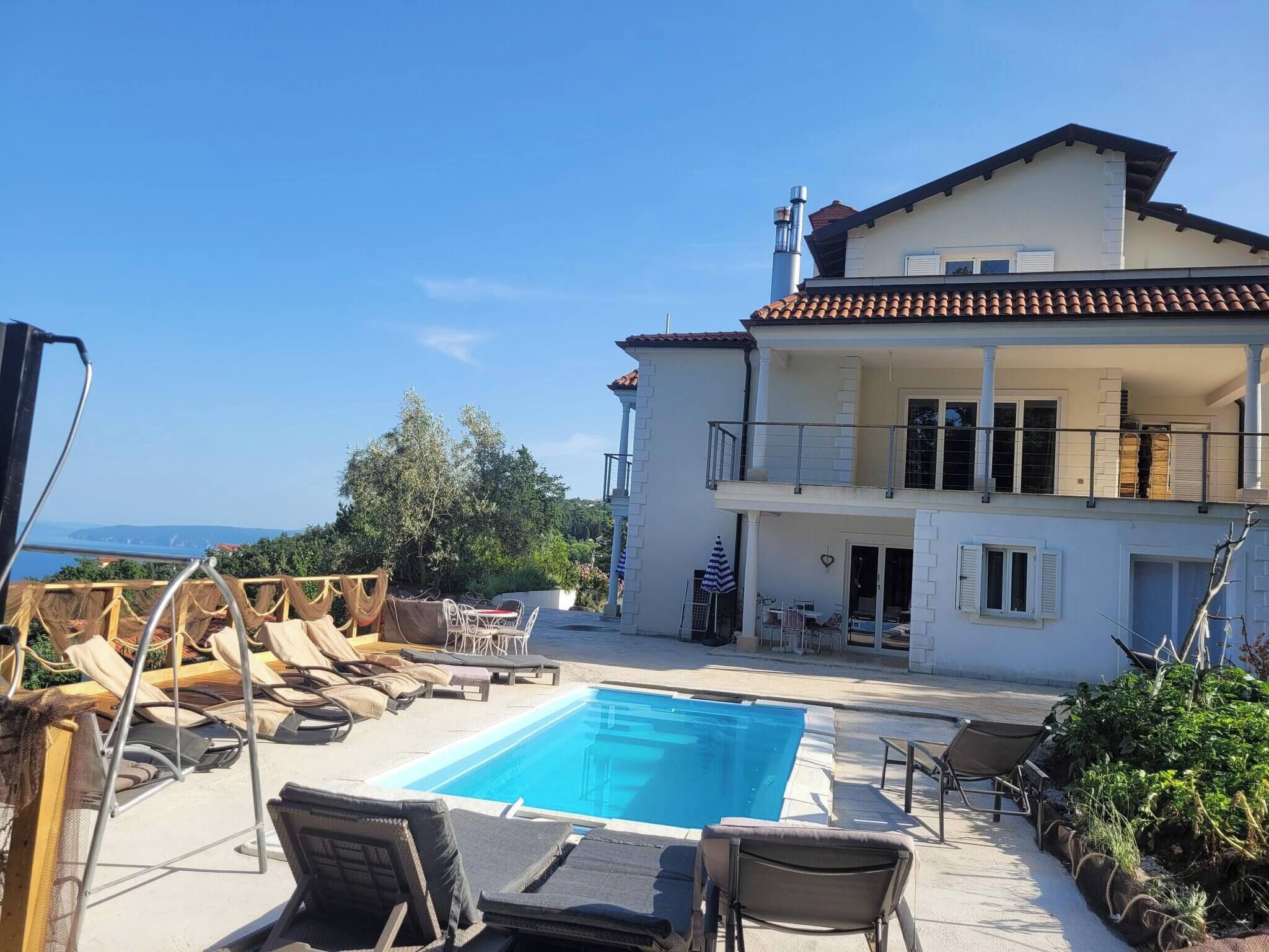 Uma casa de dois andares com piscina, área de estar externa e vista para o mar.