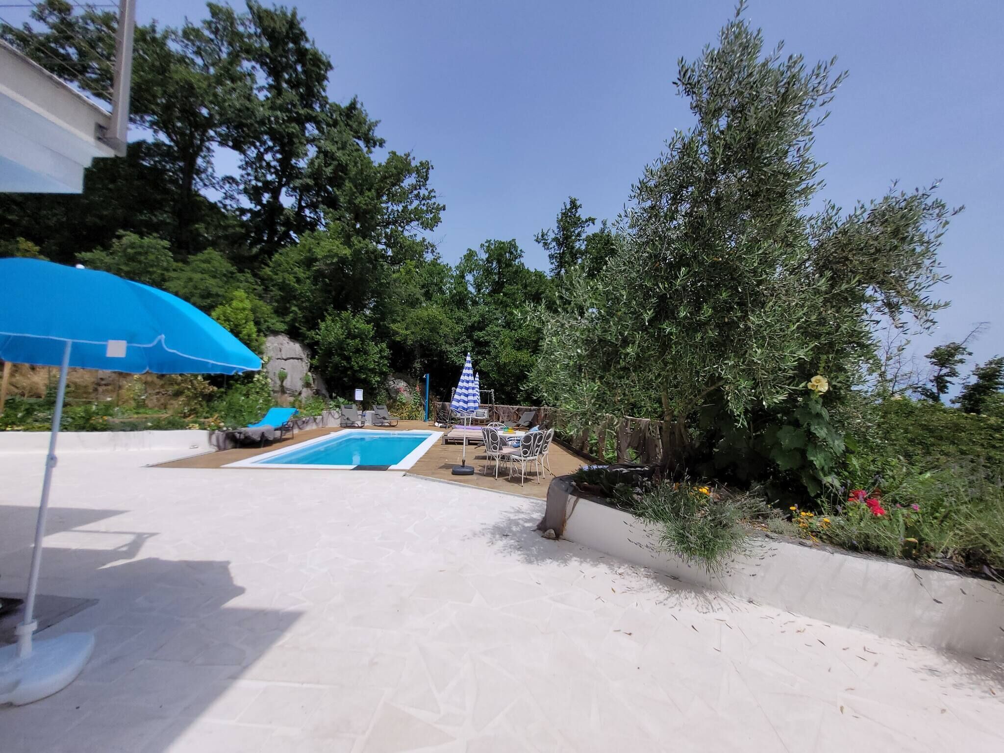 Piscina com espreguiçadeiras, um guarda-sol azul e um espaço de refeições com mobiliário de exterior.