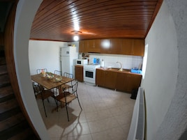 Uma cozinha com armários de madeira, uma mesa de jantar com cadeiras, uma geladeira, um micro-ondas e um fogão.