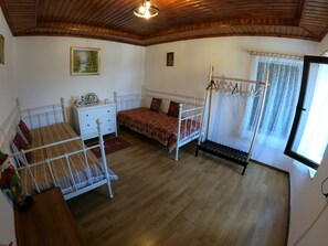 Quarto com teto de madeira, cama com colcha estampada, cômoda, um banquinho e janela com cortinas.