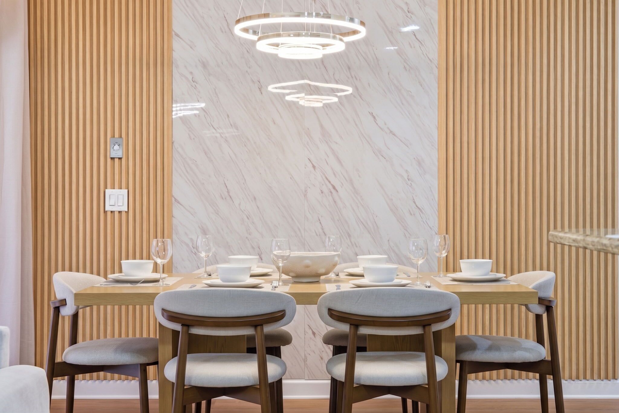 Uma sala de jantar com uma mesa de madeira posta para quatro pessoas, rodeada por cadeiras estofadas.