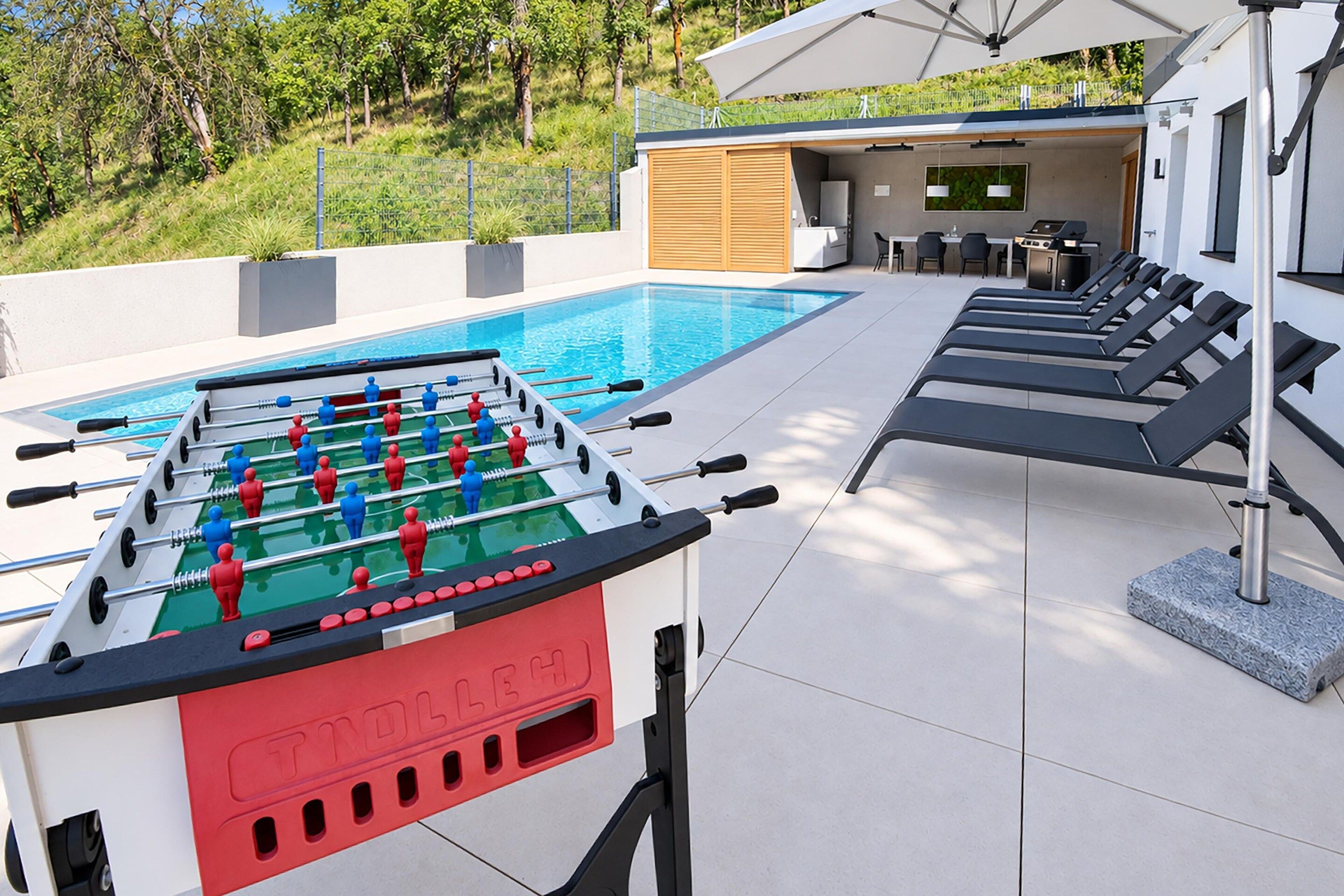 Uma área na piscina com mesa de futebol, cadeiras de descanso e um espaço coberto para sentar.