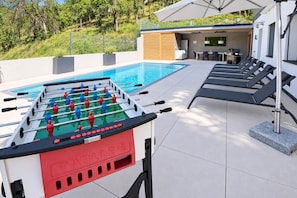 Uma área na piscina com mesa de futebol, cadeiras de descanso e um espaço coberto para sentar.