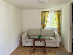 Quarto com sofá, uma mesa de madeira pequena e janela com cortinas.