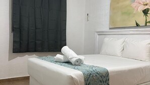 Quarto de hotel com uma cama, uma janela com cortinas escuras, um aparelho de ar condicionado e um quadro de uma flor na parede.