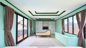 Quarto com cama, sofá, televisão e janelas amplas.
