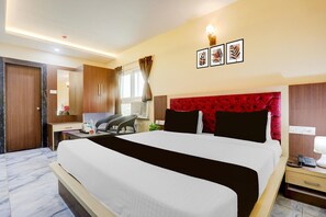 Quarto de hotel com cama, escrivaninha, cadeira e cabeceira vermelha.