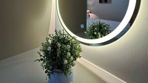 Casa de banho com espelho redondo, planta em vaso e luz embutida.