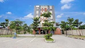 Um edifício moderno com uma placa na fachada que diz 'INAWASENA', rodeado por uma área pavimentada com árvores e céu limpo.