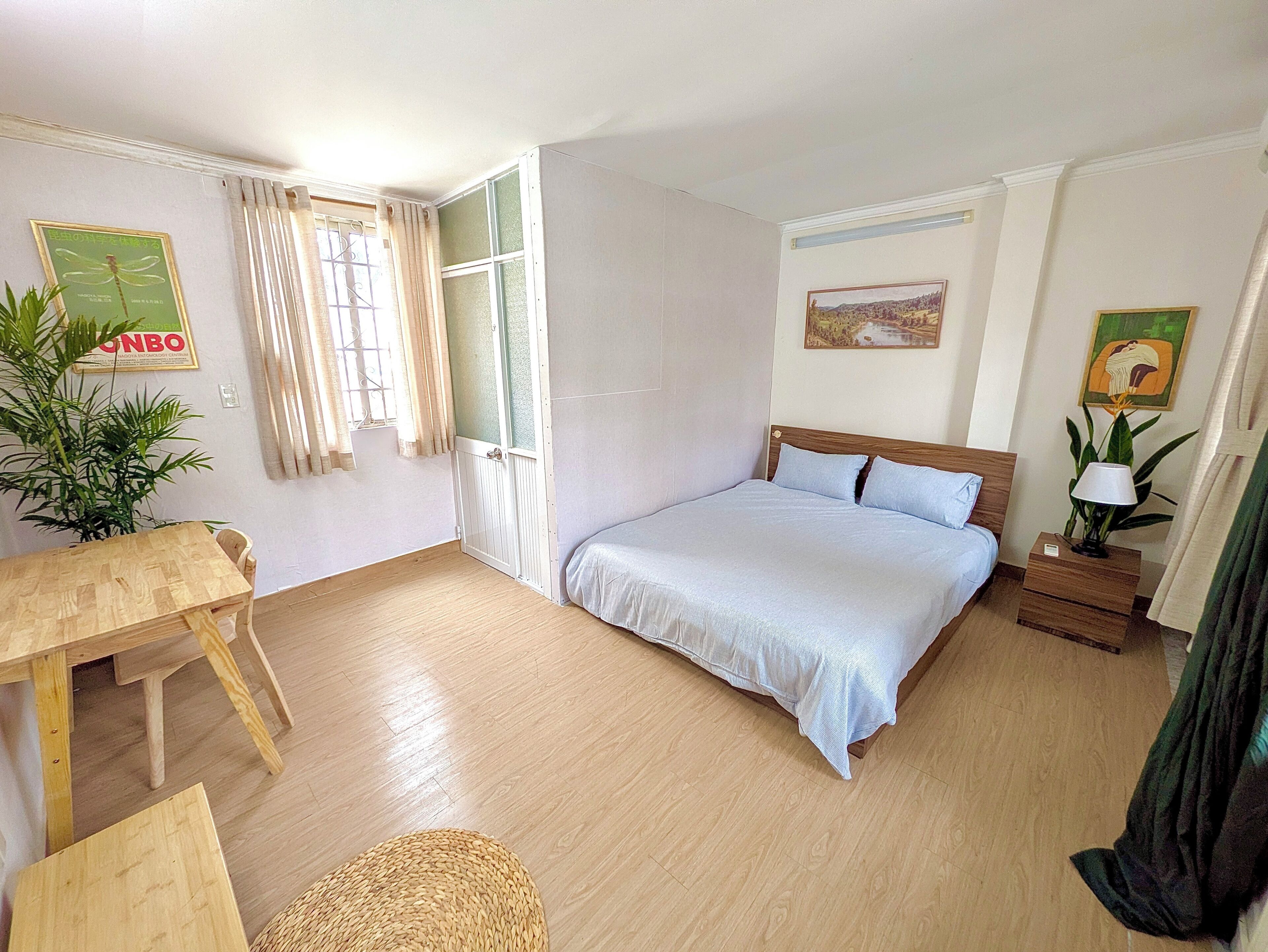 Quarto com cama, mesa de madeira, cadeira, janela com cortinas e um quadro pendurado na parede.