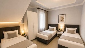 Quarto de hotel com duas camas, um guarda-roupa, uma mesa de cabeceira com abajur e uma obra de arte emoldurada na parede.