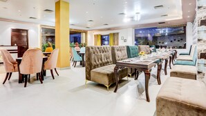 Um hall de hotel moderno com área de refeições, sofás e uma grande janela.