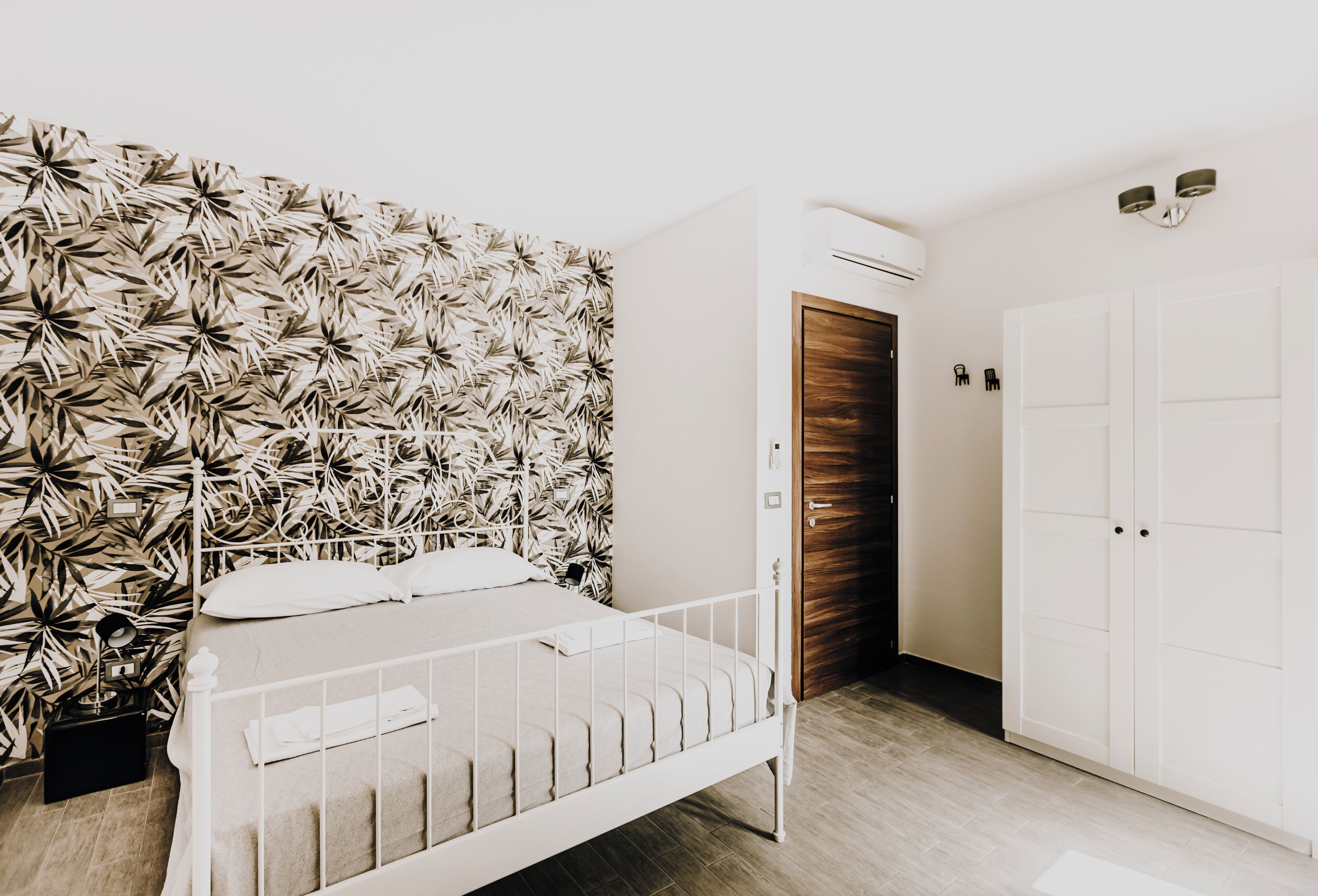 Quarto com cama, guarda-roupa, ar condicionado e parede com padrão de folhas.