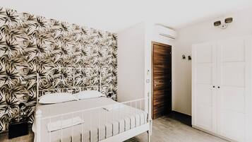 Quarto com cama, guarda-roupa, ar condicionado e parede com padrão de folhas.