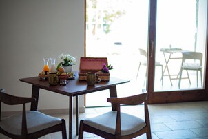 Uma mesa de jantar com cadeiras, um cesto, um vaso com flores e uma janela com vista para o exterior.