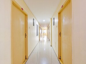 Um corredor comprido e estreito, com portas em ambos os lados, placas com números acima das portas e piso de azulejos.
