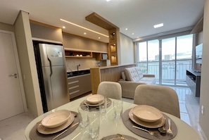 Uma cozinha moderna com eletrodomésticos embutidos, uma sala de jantar com mesa posta para quatro pessoas e uma varanda com vista.