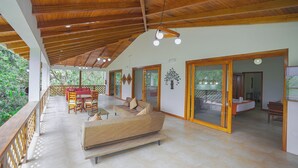Uma sala de estar ampla com teto de madeira alto, um sofá, uma mesa de jantar com cadeiras e vista para o exterior.