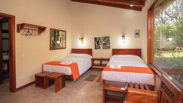 Quarto com duas camas, cabeceiras de madeira, uma mesinha e um banco.