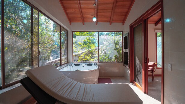 Um quarto de spa com uma banheira grande, uma mesa de massagem e vista para o exterior por grandes janelas.