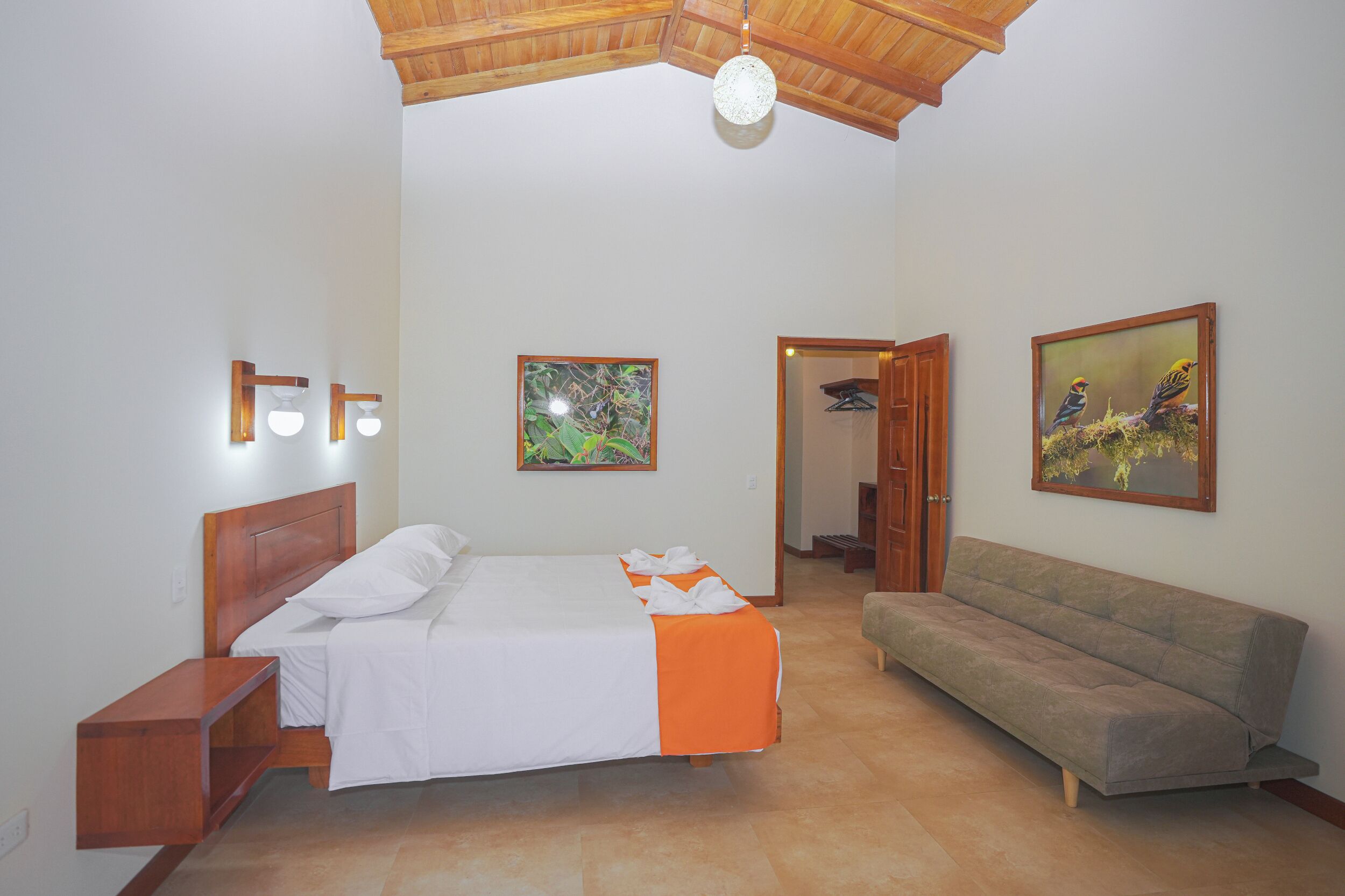 Quarto com cama, sofá, mesa de cabeceira e duas luminárias fixadas na parede.
