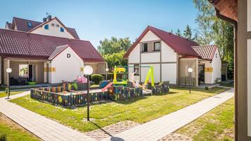 Um bairro residencial com casas, um caminho pavimentado e uma área de recreação infantil com brinquedos coloridos.