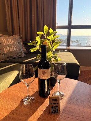 Uma mesa com uma garrafa de vinho, duas taças de vinho, um vaso de planta e um sinal com código QR.