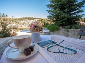 Uma mesa com xícara, pires, chocolates, um livro e copos.