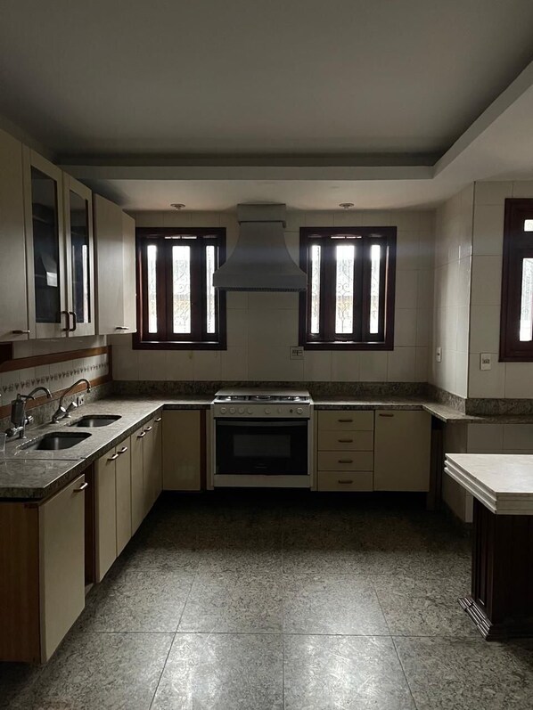 Cozinha equipada com fogão, forno, duas pias e uma janela com grade decorativa.