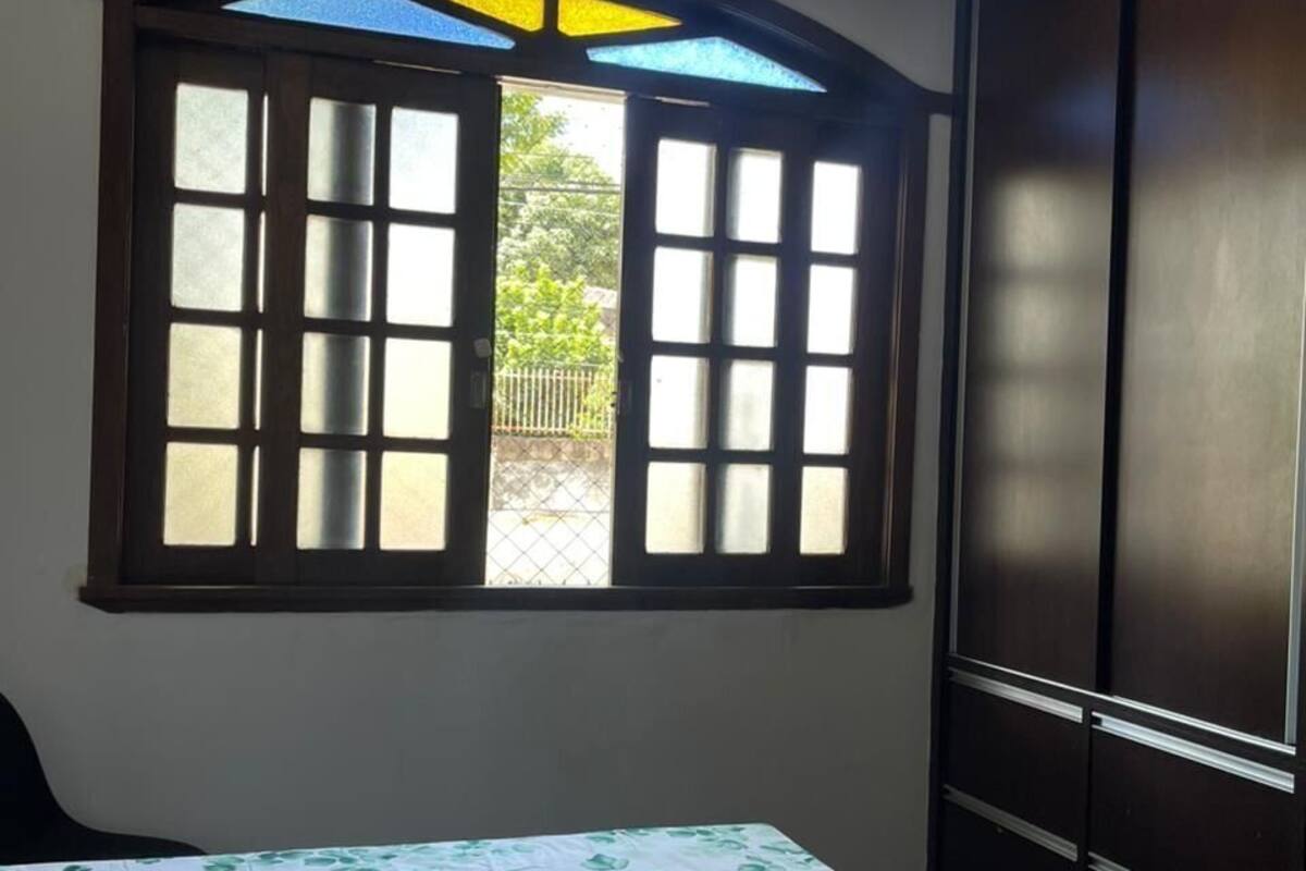Quarto com cama, janela com venezianas abertas e guarda-roupa.