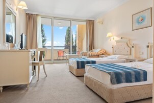 Quarto de hotel com duas camas, uma escrivaninha, uma cadeira e vista para o exterior.