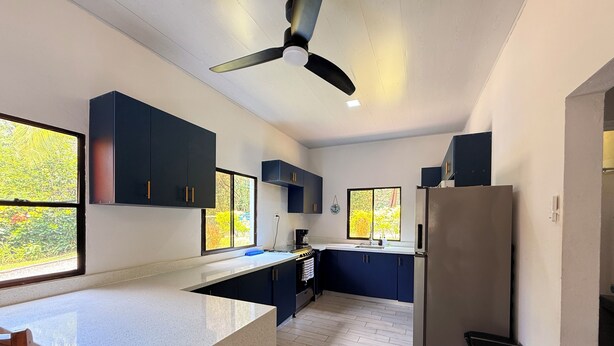 Cozinha moderna com armários escuros, geladeira de aço inoxidável, piso de madeira e ventilador de teto.