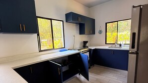 Uma cozinha moderna com armários azul escuro, bancada branca e uma geladeira de aço inoxidável.