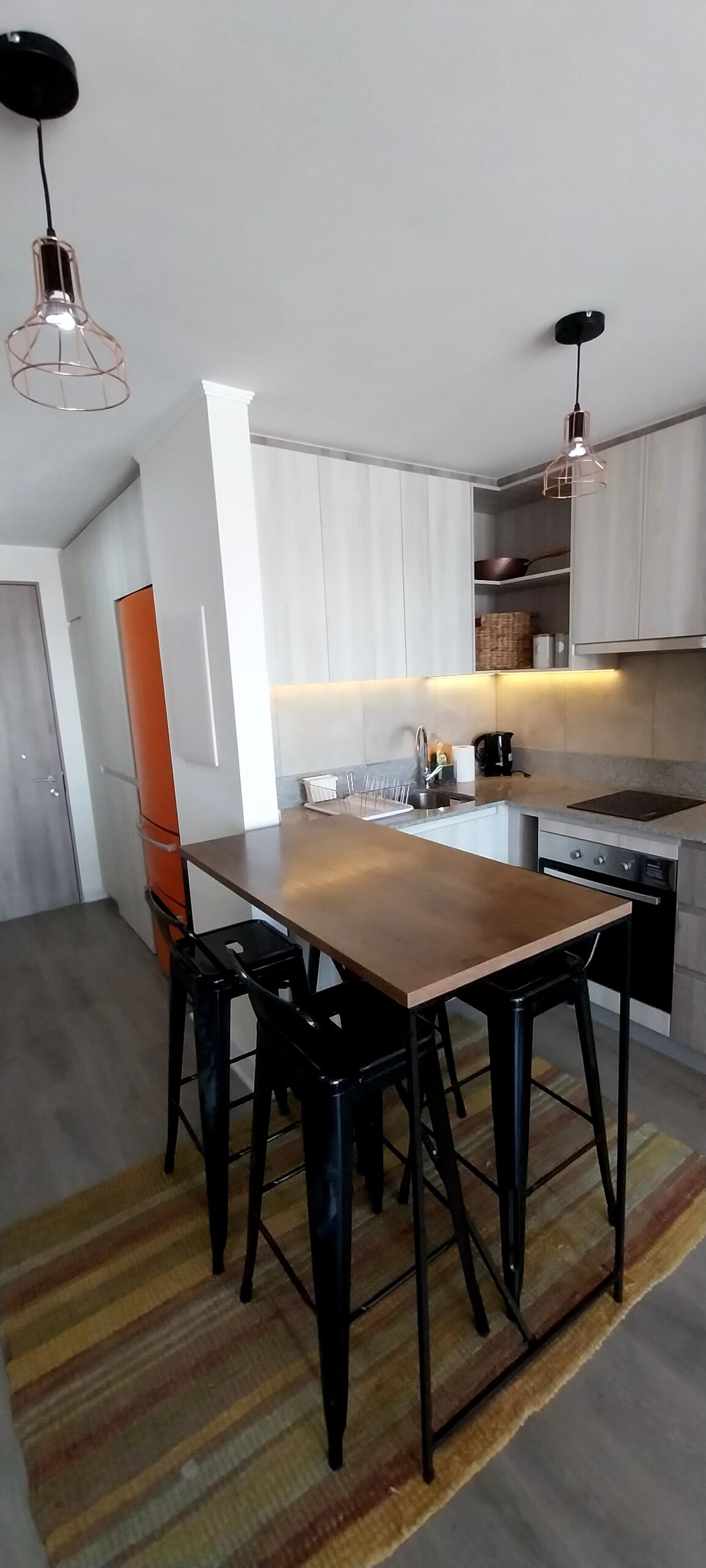 Uma cozinha moderna com uma mesa de madeira, cadeiras pretas e um tapete listrado.