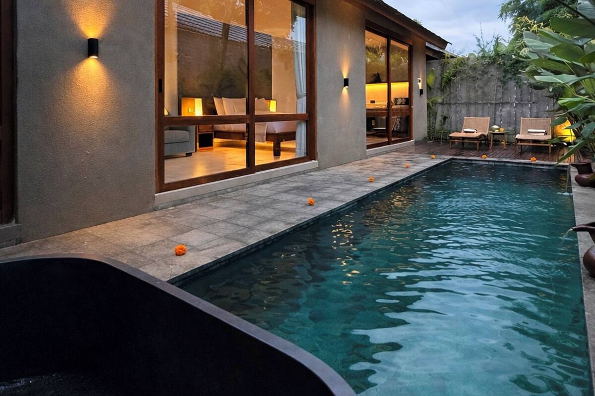 Piscina com superfície de água límpida, adjacente a um edifício com grandes janelas e um terraço com cadeiras.
