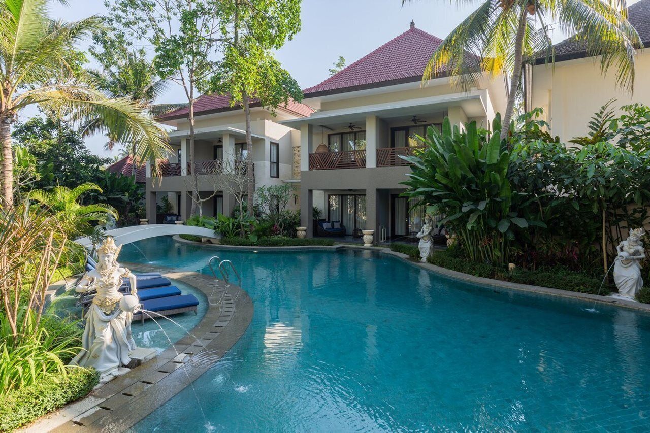 Um resort com piscina, uma estátua e um edifício de dois andares com varandas.