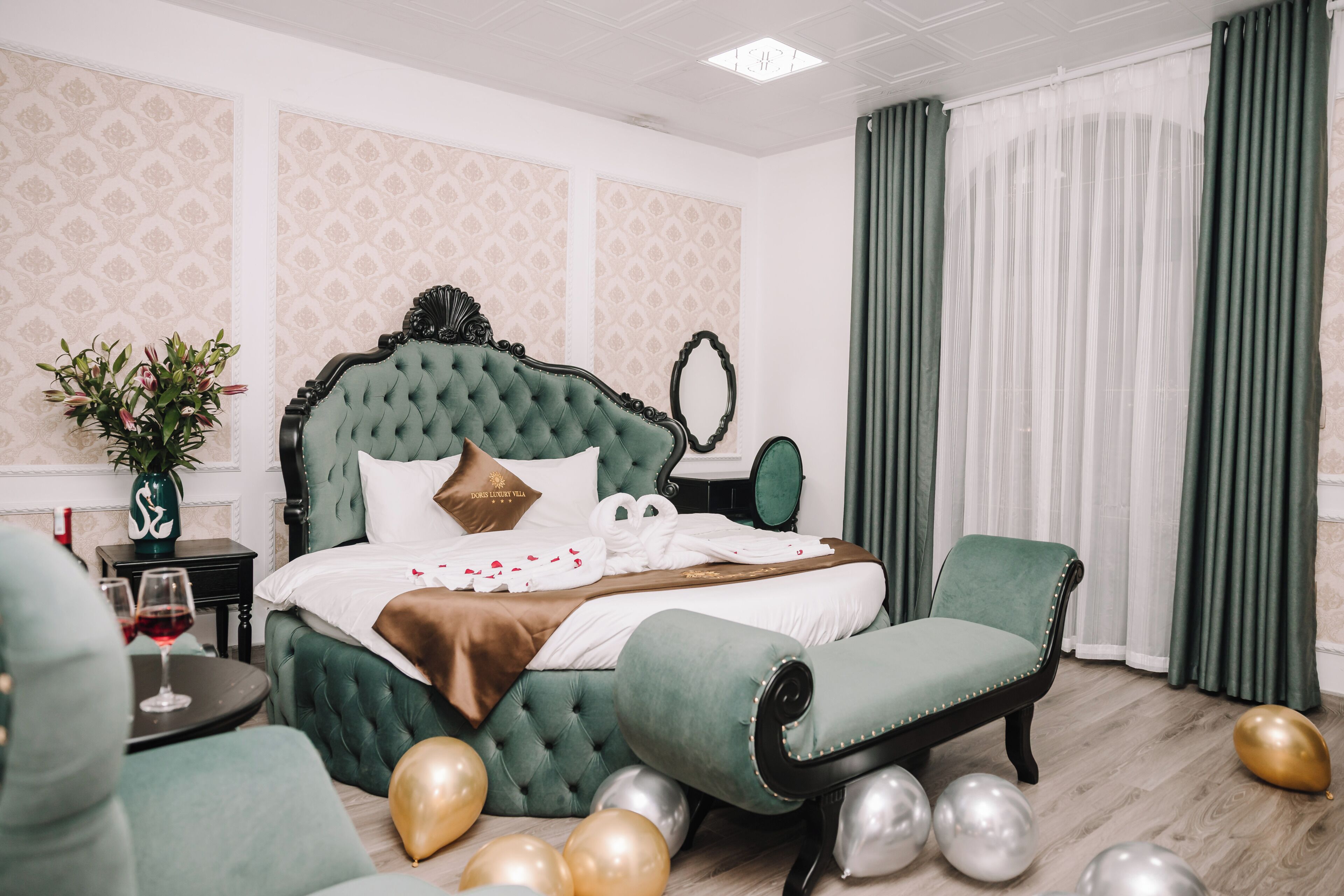 Quarto com cabeceira estofada, cama com roupa de cama branca, poltrona verde e balões no chão.