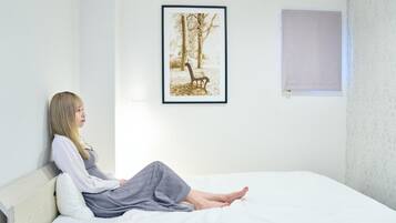 Um quarto com uma cama, um quadro na parede e uma janela com persiana.