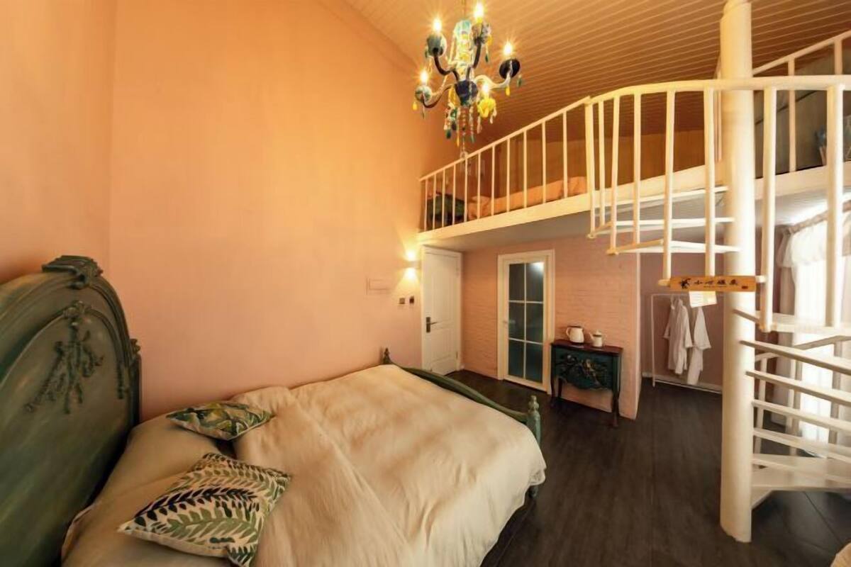 Quarto com cama, lustre, escada e porta que dá para outro cômodo.