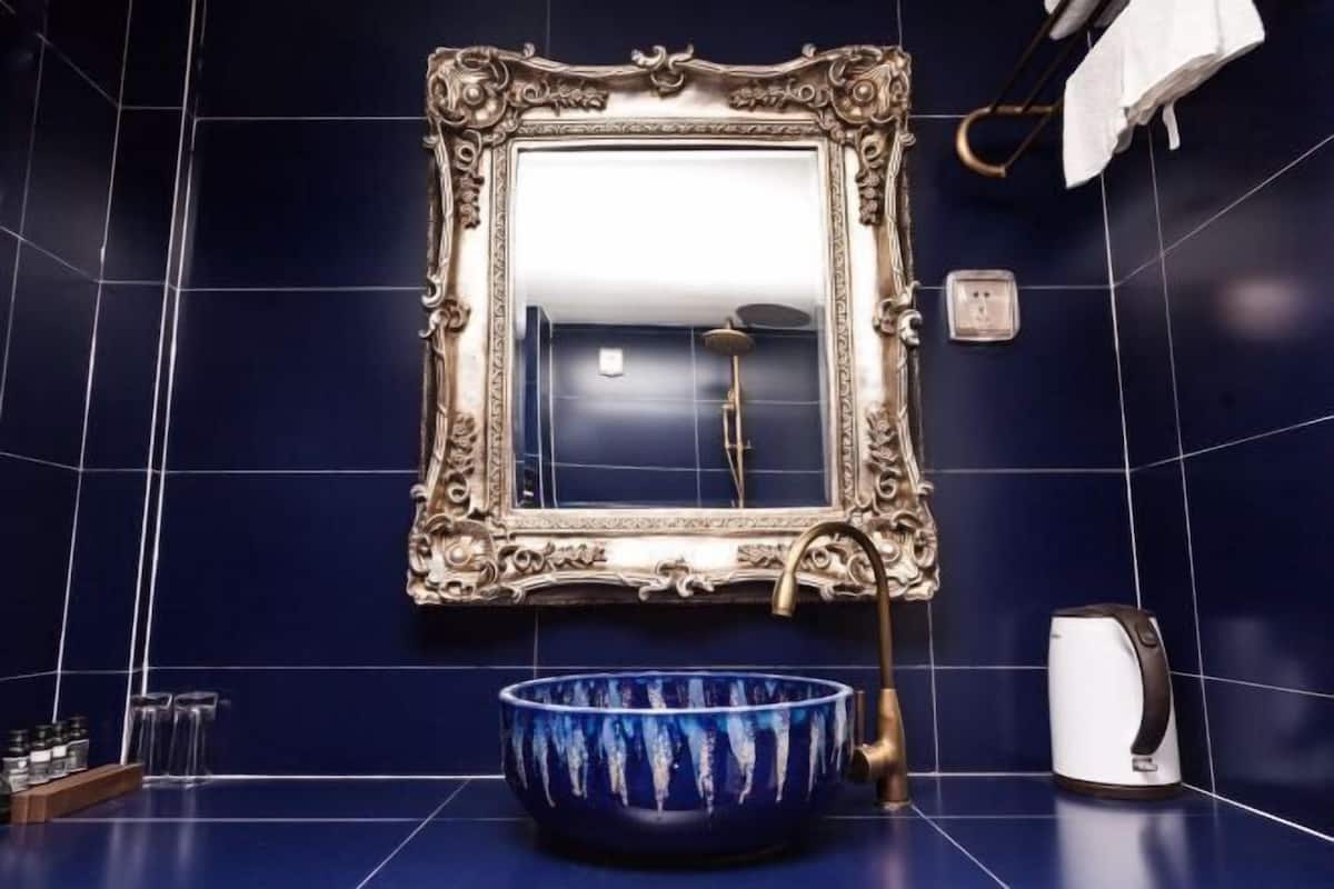 Um banheiro com um espelho grande e ricamente decorado, uma pia azul em vaso e uma chaleira elétrica branca.