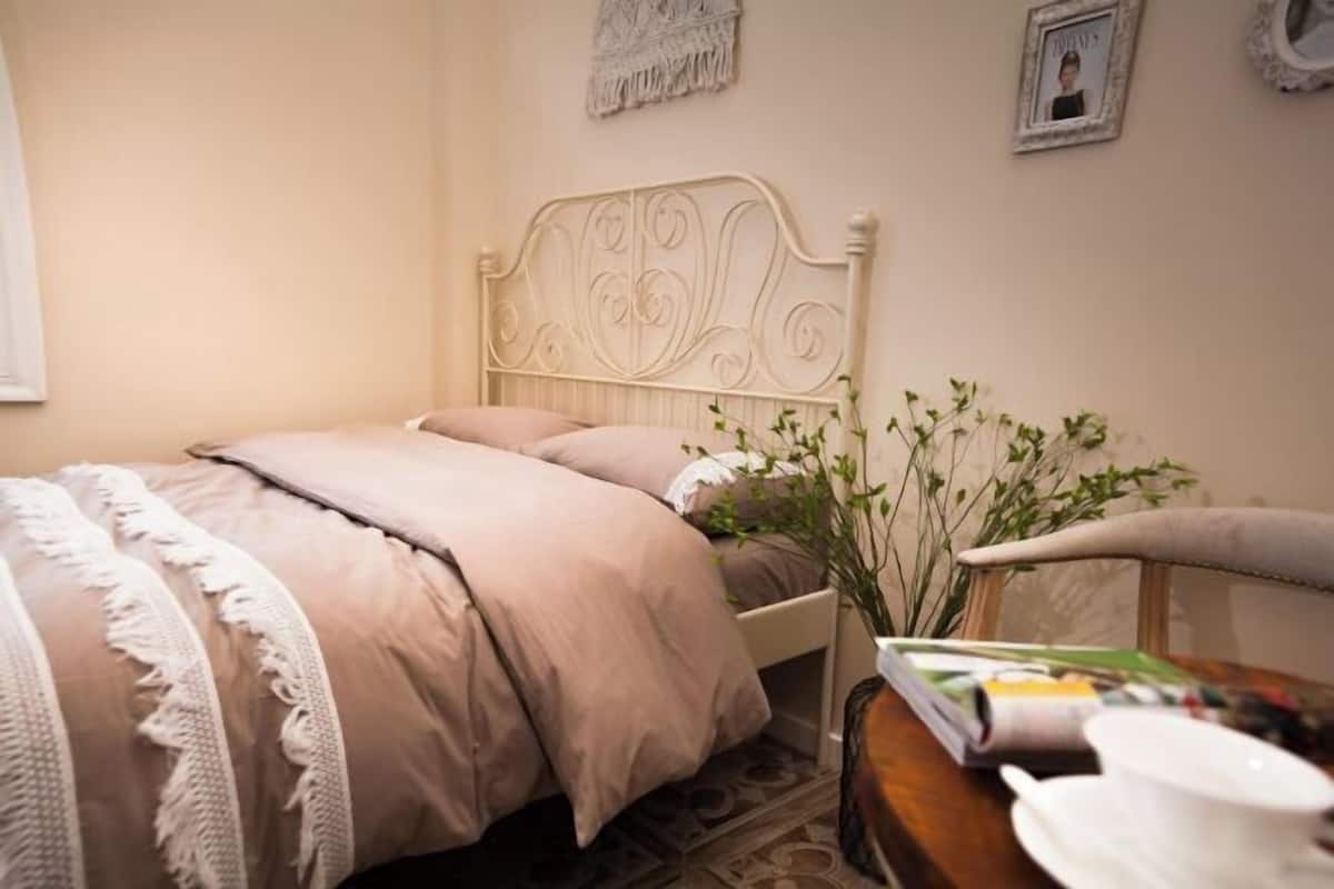 Quarto com uma cama, mesa de cabeceira com uma chávena e um livro, e uma cadeira.