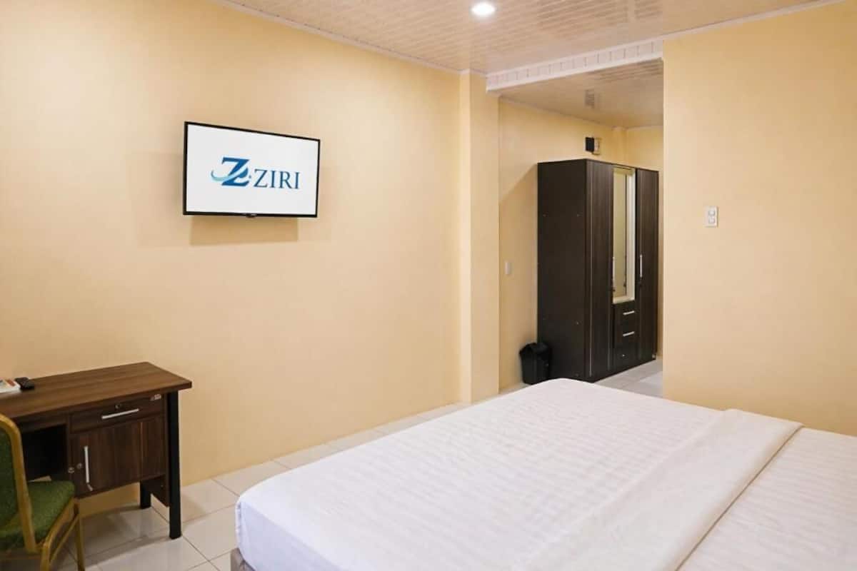 Quarto de hotel com cama, escrivaninha, guarda-roupa e um aviso ZIRI na parede.