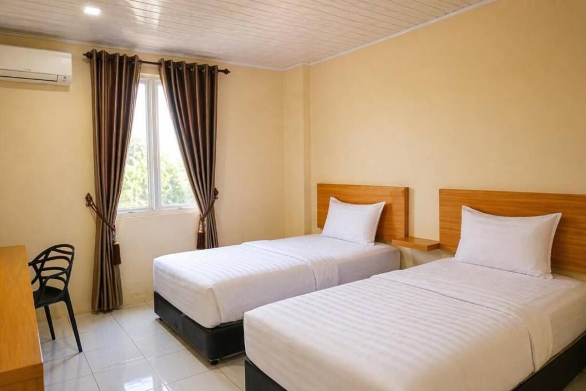 Quarto de hotel com duas camas, uma escrivaninha, uma cadeira e um ar condicionado.