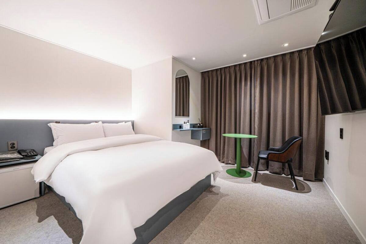Quarto de hotel moderno com uma cama grande, uma escrivaninha, uma cadeira, uma mesa verde e um banheiro com espelho.