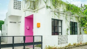 Um edifício moderno com fachada branca, porta rosa e parede coberta por trepadeiras verdes.