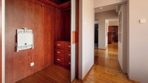 Quarto com piso de madeira, guarda-roupa com várias gavetas, uma caixa elétrica branca e uma porta que dá para outro cômodo.