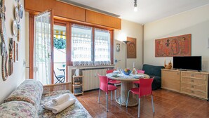 Um quarto com uma cama, uma mesa de jantar com cadeiras, uma televisão e uma janela com cortinas.