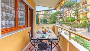 Varanda com mesa posta para refeições, uma cadeira e vista para a rua e edifícios.