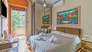 Quarto de hotel com uma cama, uma mesa com garrafa e copos, um espelho e um quadro na parede.