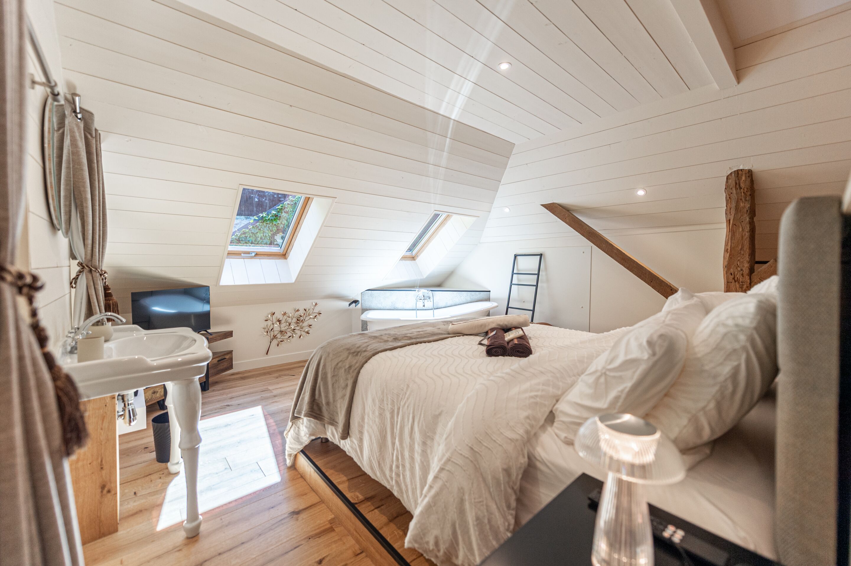Quarto com claraboia, mesa de cabeceira, cama, janela e banheiro com pia e espelho.